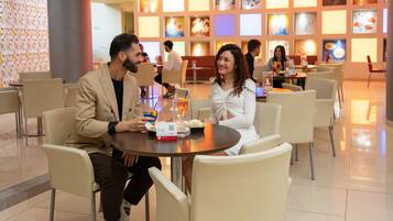 Um café moderno com um design limpo e minimalista, apresentando uma mesa redonda central com cadeiras, uma parede decorativa com obras de arte emolduradas e um chão polido.