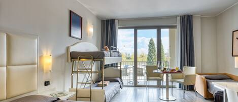 Quarto de hotel com uma cama beliche, uma escrivaninha com cadeira, uma mesa pequena e vista para o exterior.