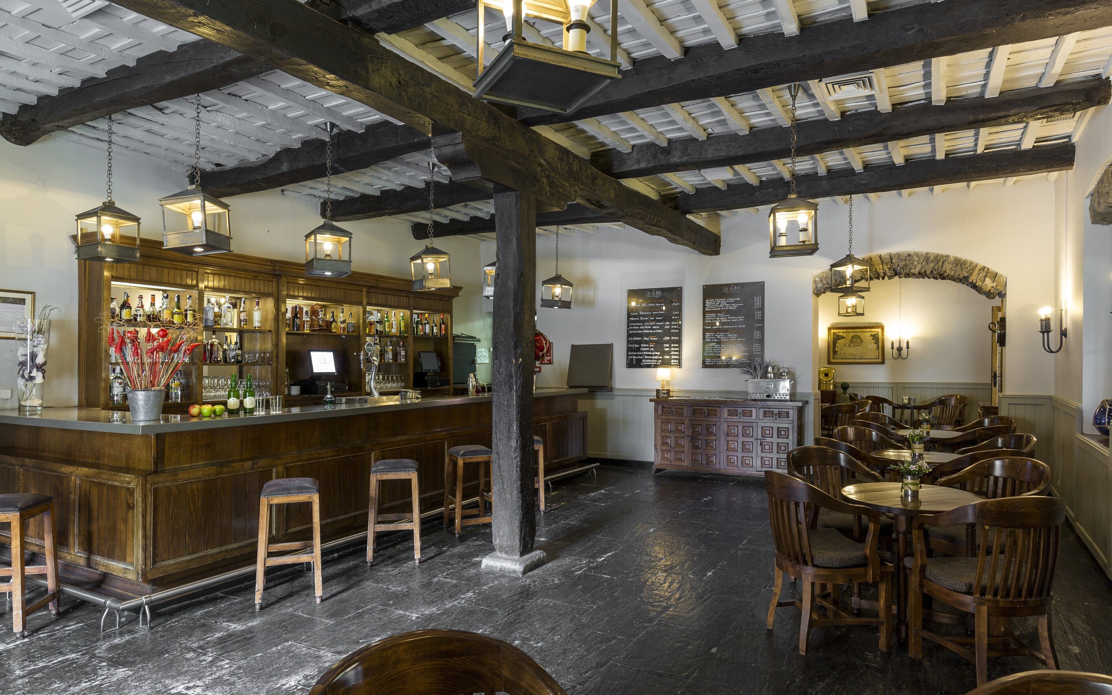 Uma área de bar com mobiliário de madeira, piso de pedra e lanternas penduradas.