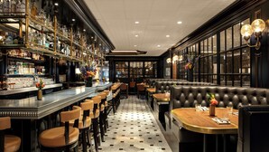 Uma área de bar com balcão extenso, vários bancos e um espaço de estar com assentos tipo cabine.