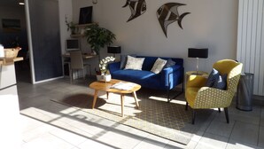Uma sala de estar moderna com um sofá azul, uma poltrona amarela, uma mesa de centro de madeira e arte decorativa na parede.