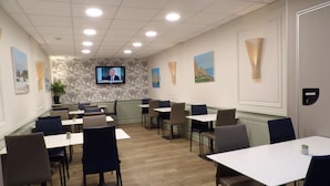 Uma sala de conferências com várias mesas e cadeiras, uma tela de televisão e arte decorativa nas paredes.