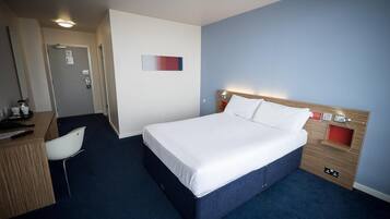 Quarto de hotel com cama, escrivaninha, cadeira e pequena mesa com prateleira vermelha.