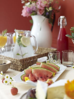 Uma mesa com melancia fatiada, um jarro, copos e um vaso com flores.