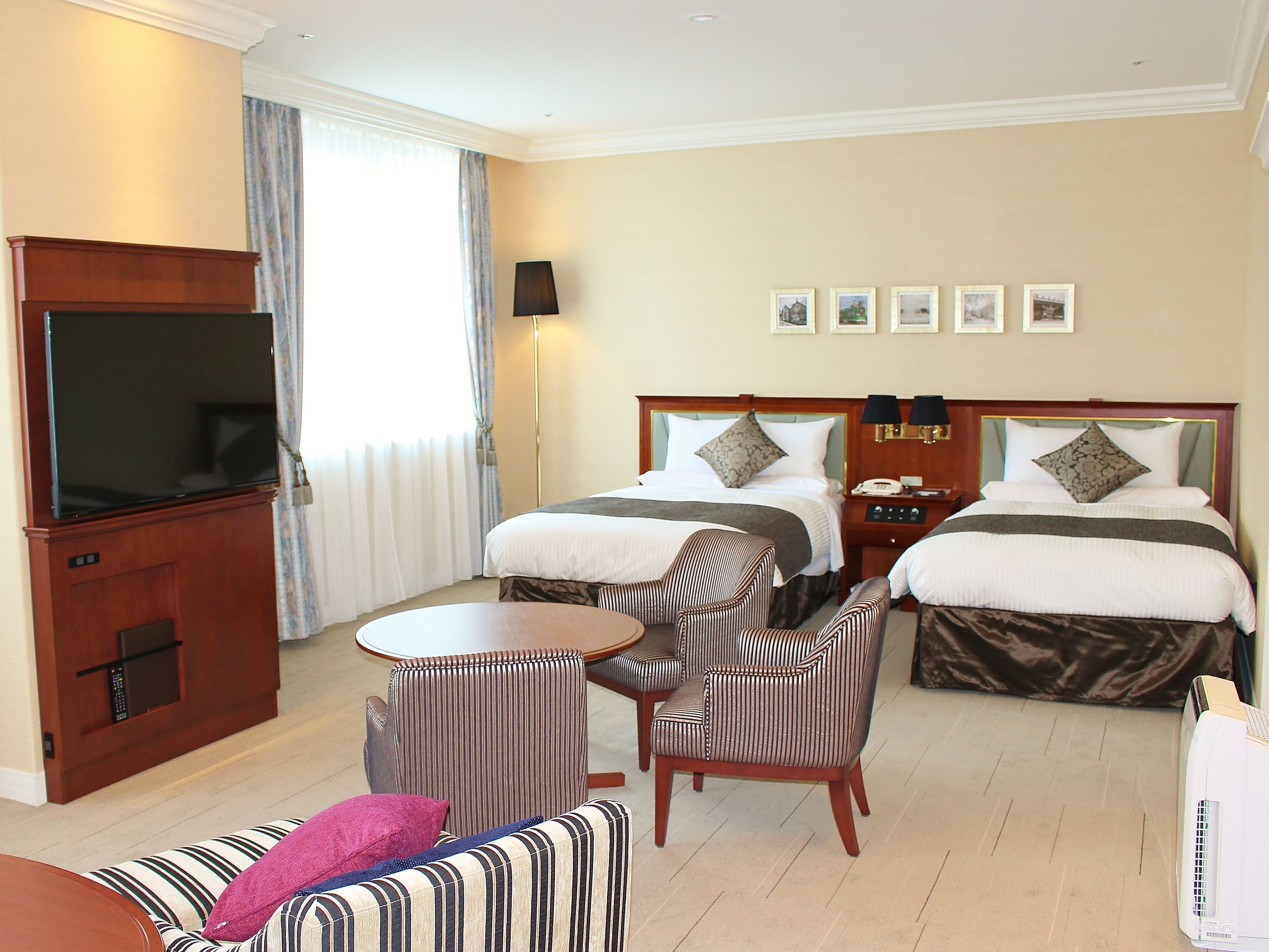 Quarto de hotel com duas camas, uma televisão, uma escrivaninha e uma cadeira.