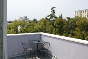 Varanda com duas cadeiras e uma mesa, com vista para um horizonte urbano com árvores e edifícios.