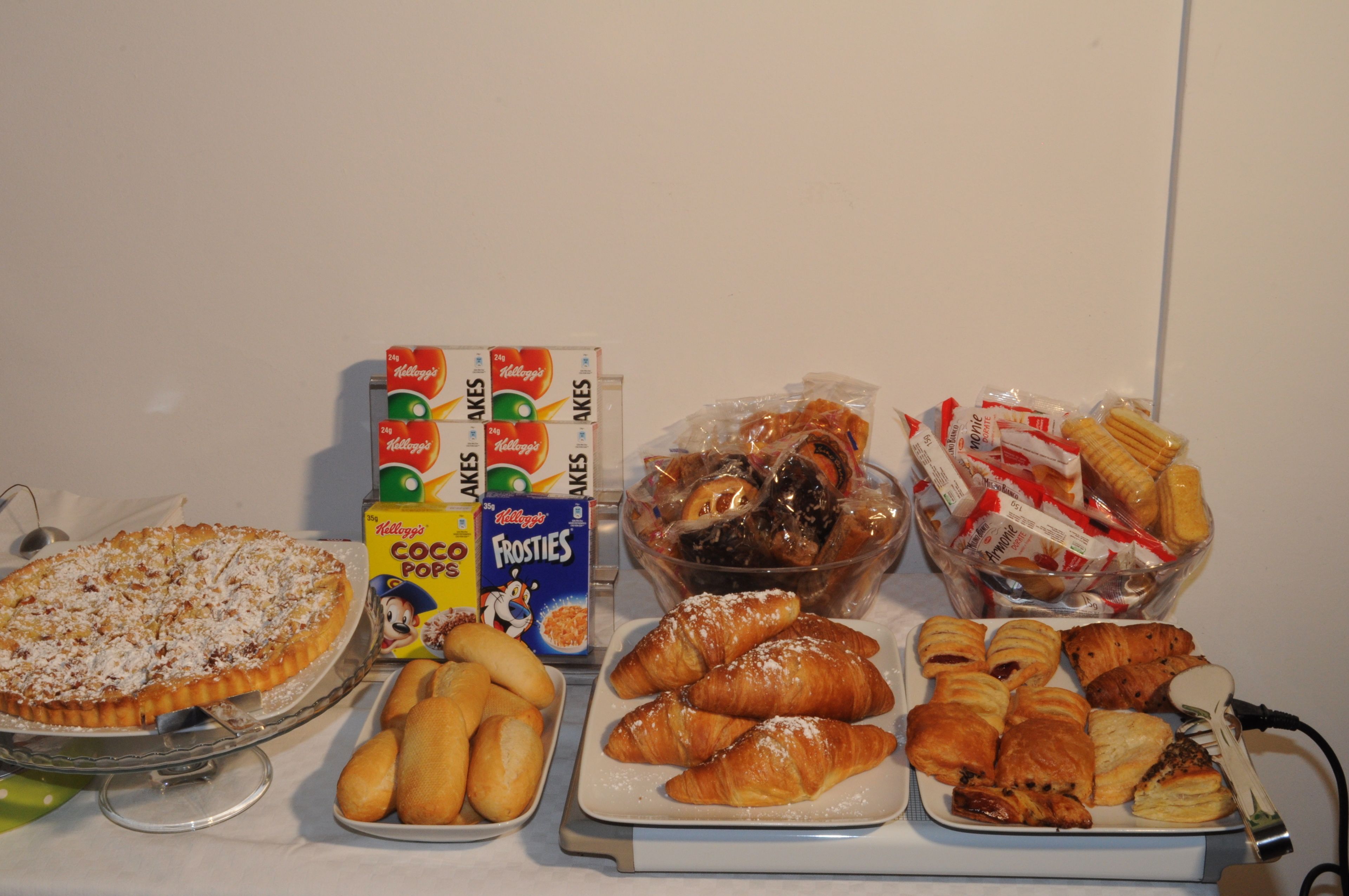Mesa de buffet com diversos alimentos, incluindo pizza, croissants e lanches embalados.