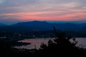 Vista noturna de um horizonte urbano com montanhas ao fundo e um corpo de água em primeiro plano.