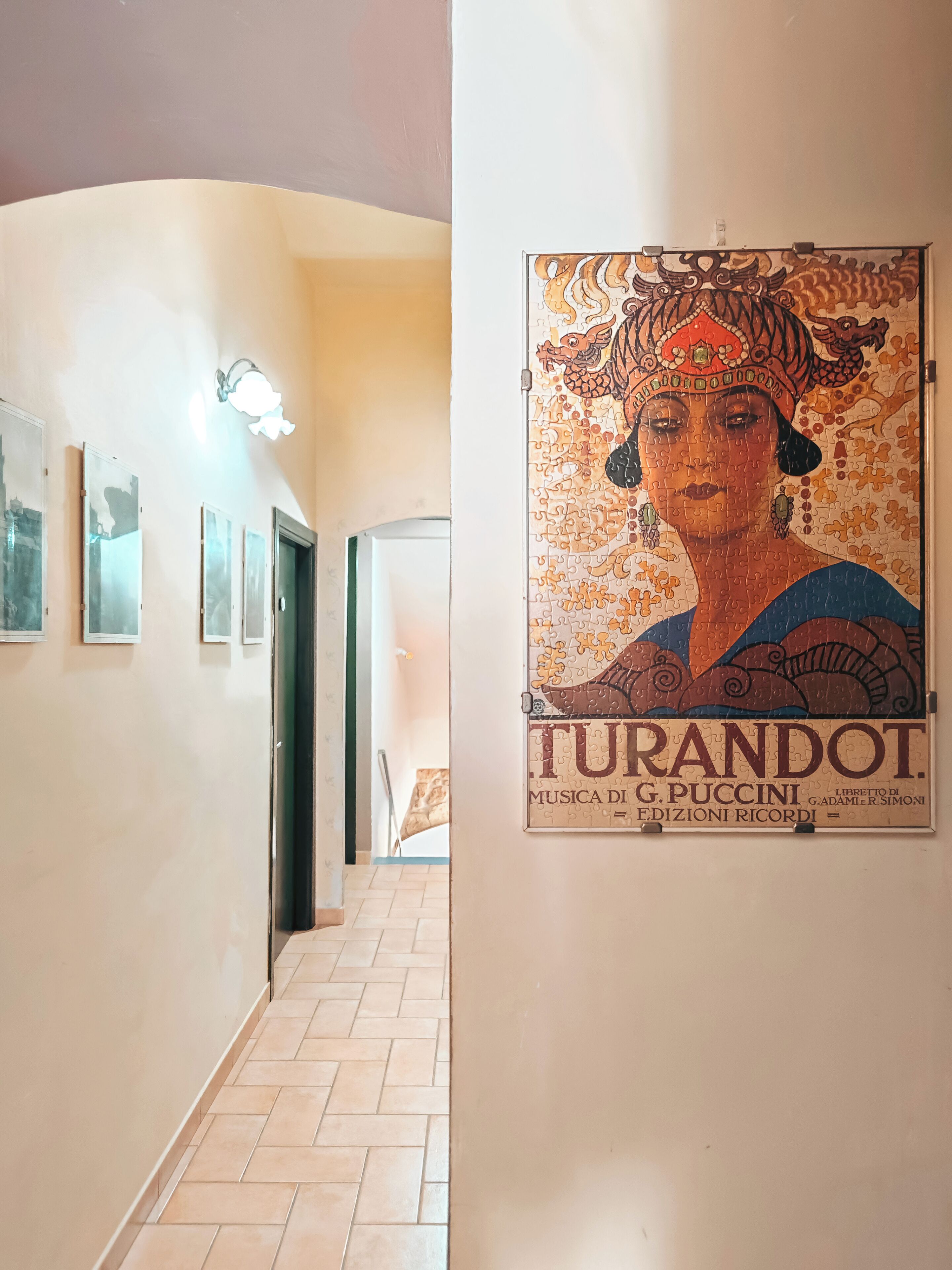 Um corredor com um cartaz fixado na parede de uma mulher vestida com traje tradicional, uma porta e quadros na parede.