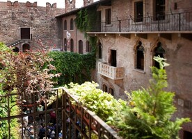 Um pátio com um edifício de tijolos, com janelas em arco e varandas, cercado por vegetação.