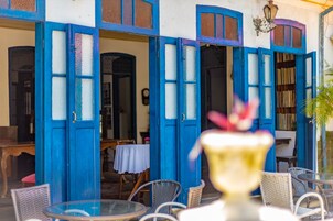 Um edifício com portas e janelas azuis, uma mesa com cadeiras e um abajur.