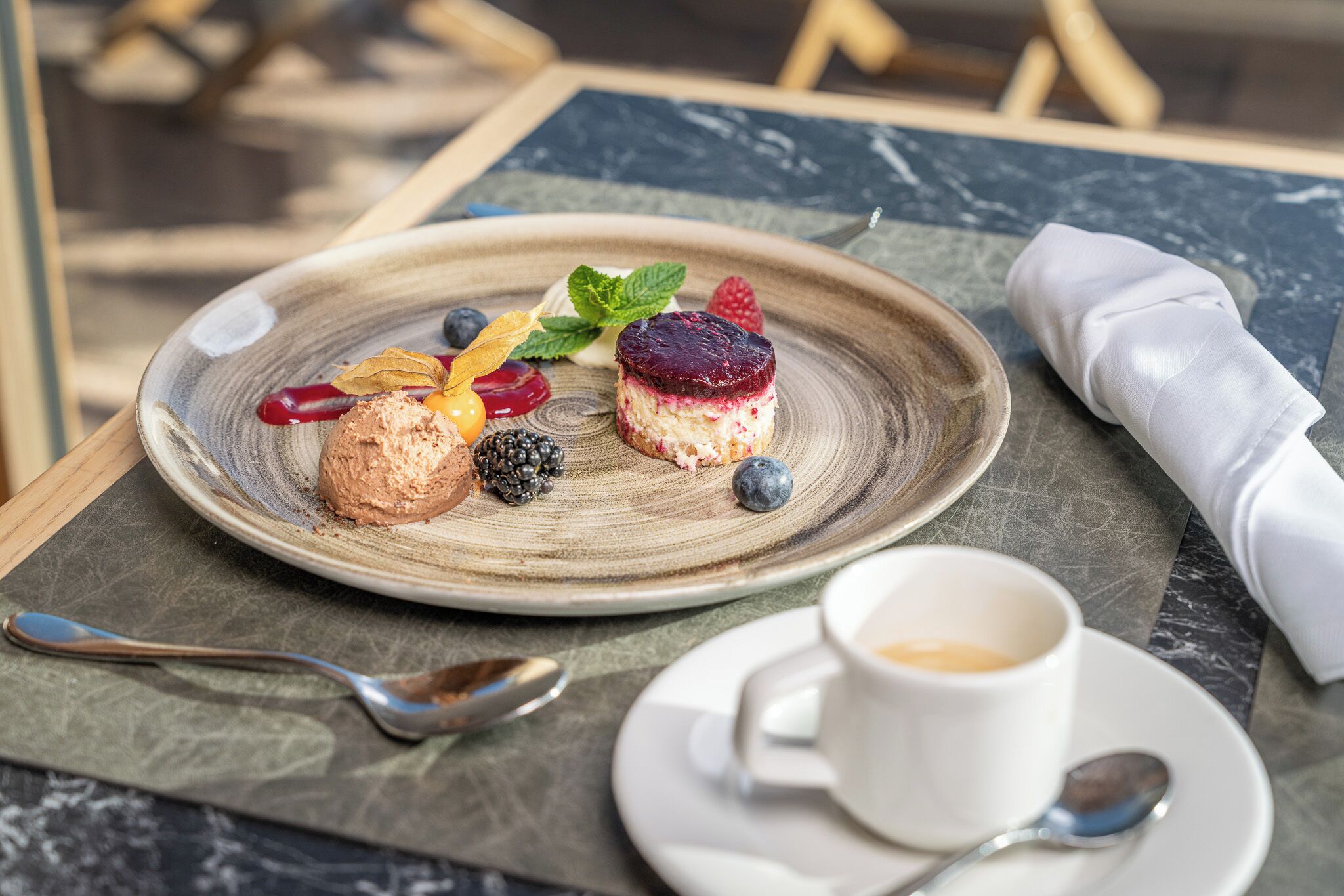 Um prato de sobremesas com doces, frutas vermelhas, uma chávena de café e uma colher sobre a mesa.