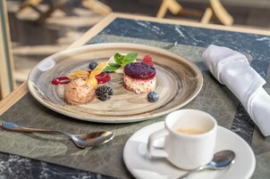 Um prato de sobremesas com doces, frutas vermelhas, uma chávena de café e uma colher sobre a mesa.