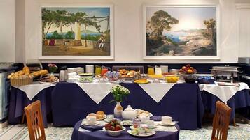 Uma sala de jantar com mesas preparadas para o café da manhã, com uma variedade de alimentos e um vaso de flores.