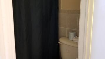 Casa de banho pequena e fechada, com sanita, um chuveiro com cortina escura e uma porta branca.