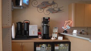 Balcão de café com duas máquinas de café, um letreiro de neon e uma geladeira cheia de bebidas.
