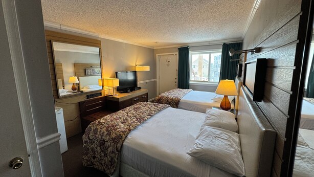 Quarto de hotel com duas camas, uma televisão, uma escrivaninha com candeeiro e um espelho grande.