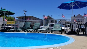 Piscina com espreguiçadeiras e guarda-sóis, cercada por uma cerca branca e bandeiras americanas.