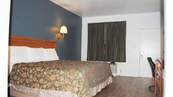 Um quarto com cama, mesa de cabeceira, abajur, janela com cortinas e porta.