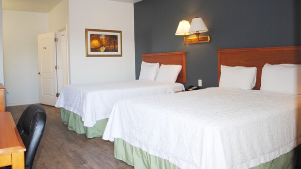 Quarto de hotel com duas camas, uma escrivaninha, uma cadeira, uma porta e uma luminária na parede.