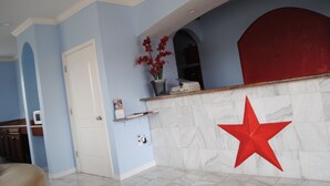 Uma área de recepção com balcão de mármore, uma decoração em forma de estrela vermelha e um vaso de planta.