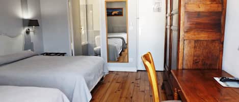 Quarto de hotel com duas camas, uma mesa de jantar de madeira, uma cadeira e um espelho refletindo o quarto.