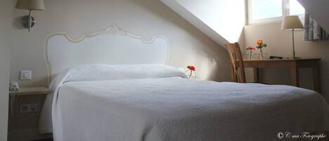Quarto com cama, escrivaninha e cadeira. Uma janela garante iluminação natural.