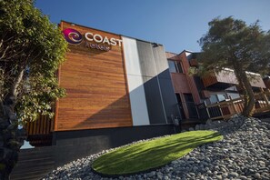 Um hotel moderno com fachada de madeira, um letreiro com a inscrição 'COAST hotels' e um gramado bem cuidado.