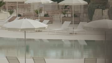 Área de piscina com espreguiçadeiras e guarda-sóis, cercada por um edifício com varandas e palmeiras.