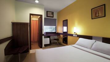 Quarto de hotel com cama, escrivaninha, cadeira e janela com cortinas.