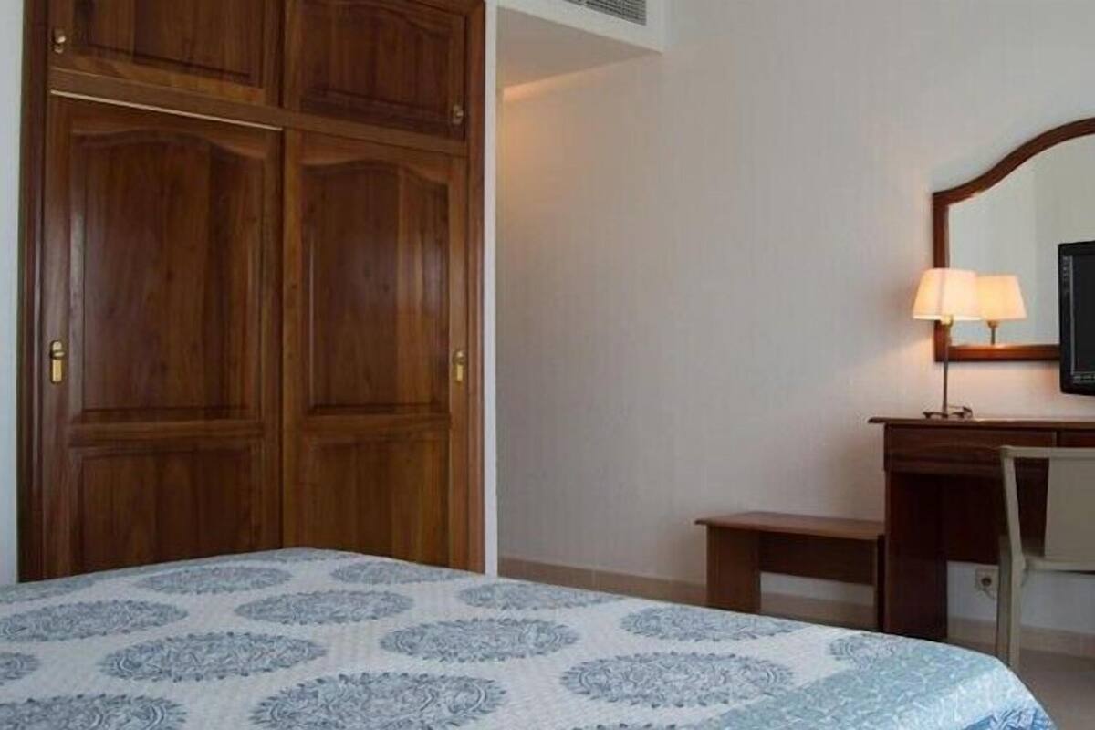 Quarto de hotel com uma cama, uma secretária, uma cadeira, uma televisão e um guarda-roupa.