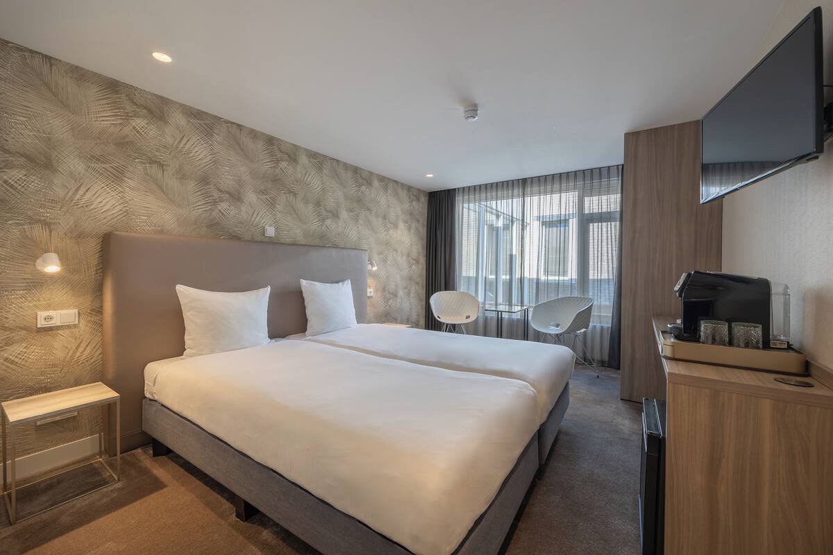 Quarto de hotel com uma cama grande, televisão, escrivaninha e uma cadeira.