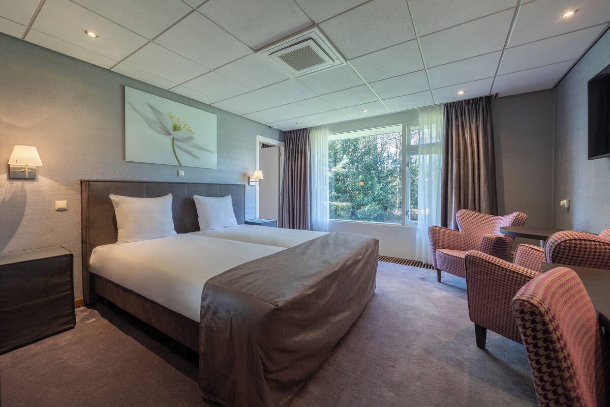 Quarto de hotel com uma cama grande, uma escrivaninha e duas poltronas.