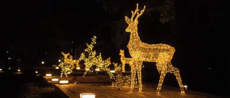 Uma grande escultura iluminada de um veado em uma plataforma de madeira, com pequenas luzes ao fundo.