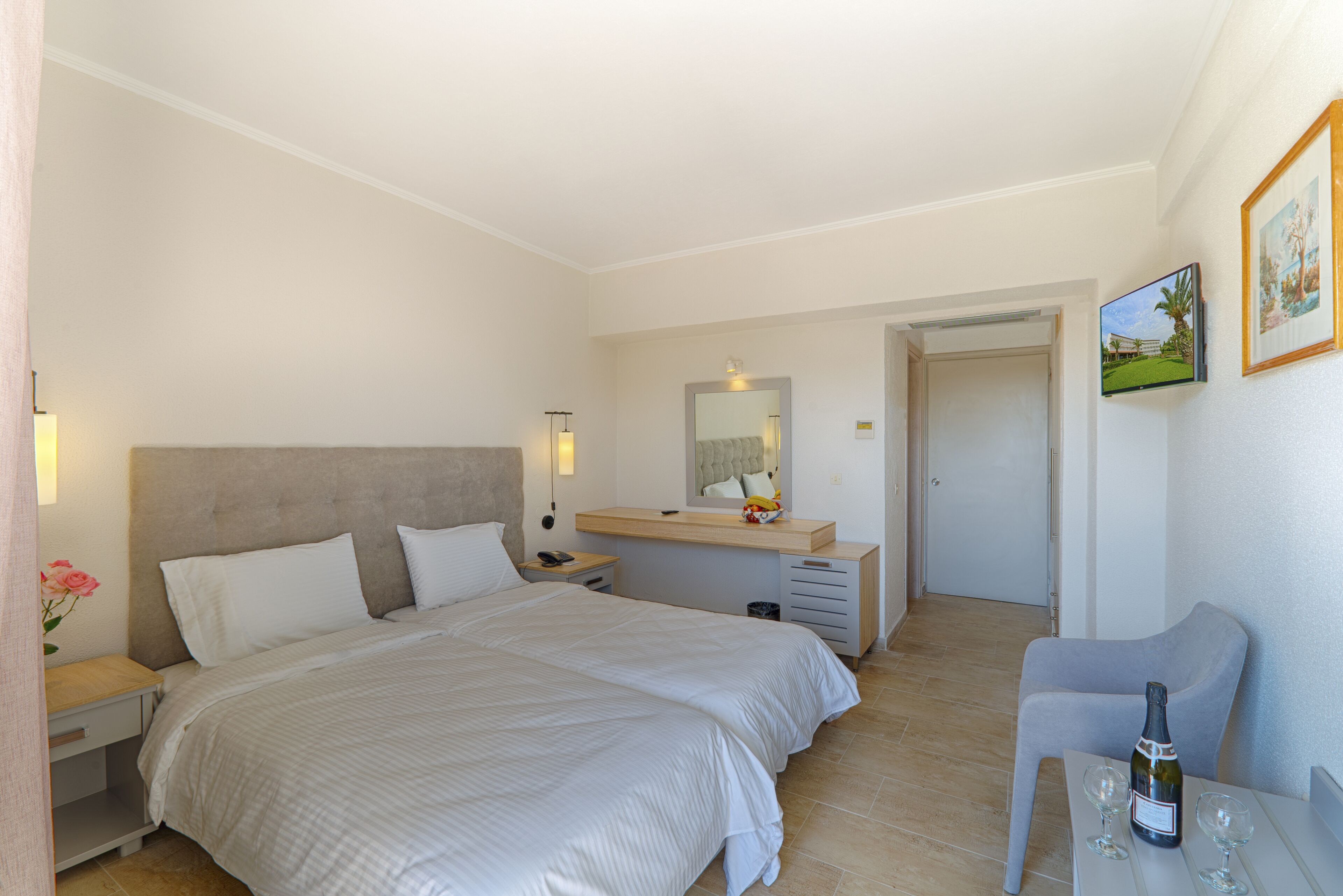 Quarto de hotel com duas camas, uma escrivaninha, uma cadeira, uma televisão e uma garrafa de champanhe.