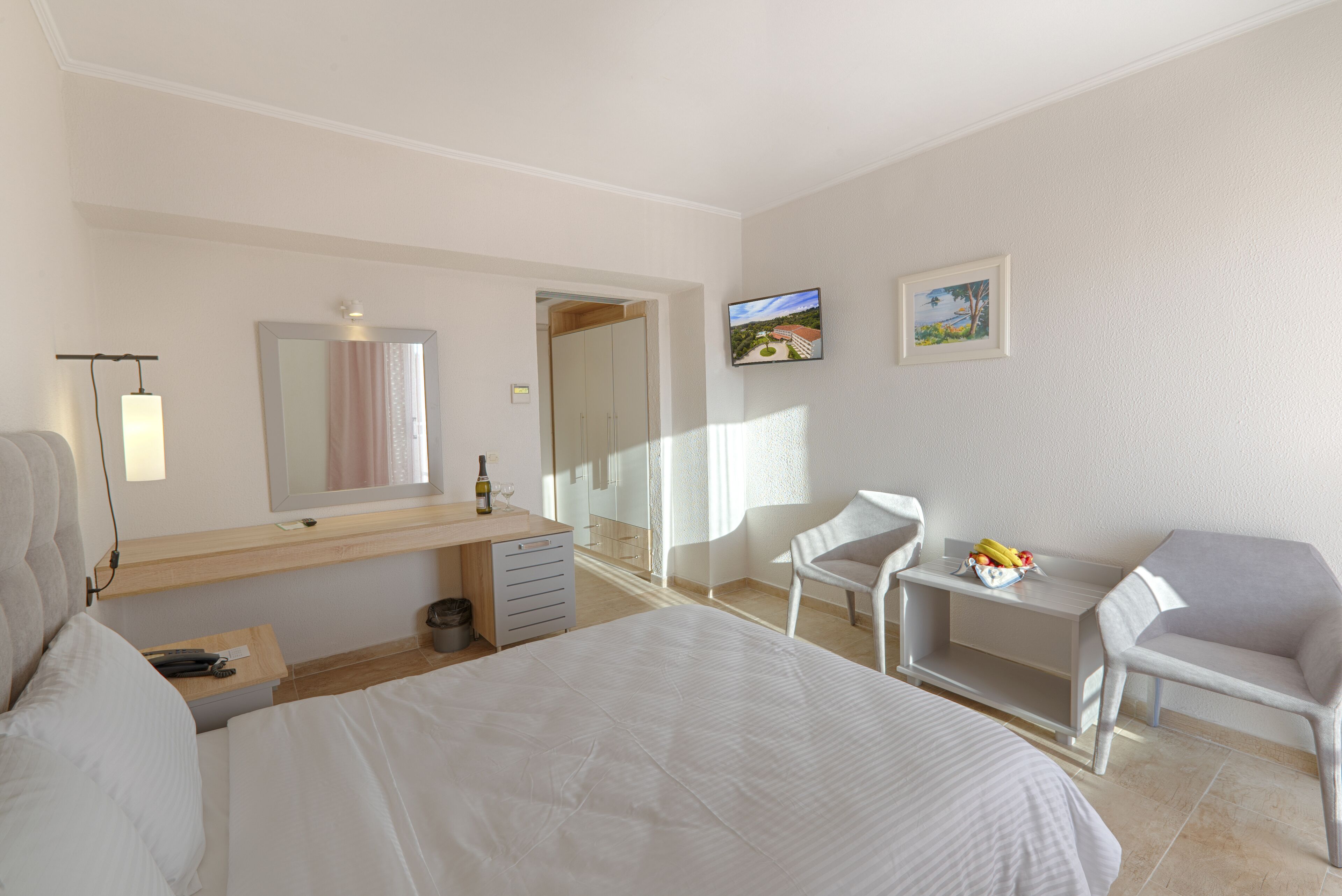 Quarto de hotel com cama, escrivaninha, cadeira, televisão e janela.