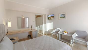 Quarto de hotel com cama, escrivaninha, cadeira, televisão e janela.