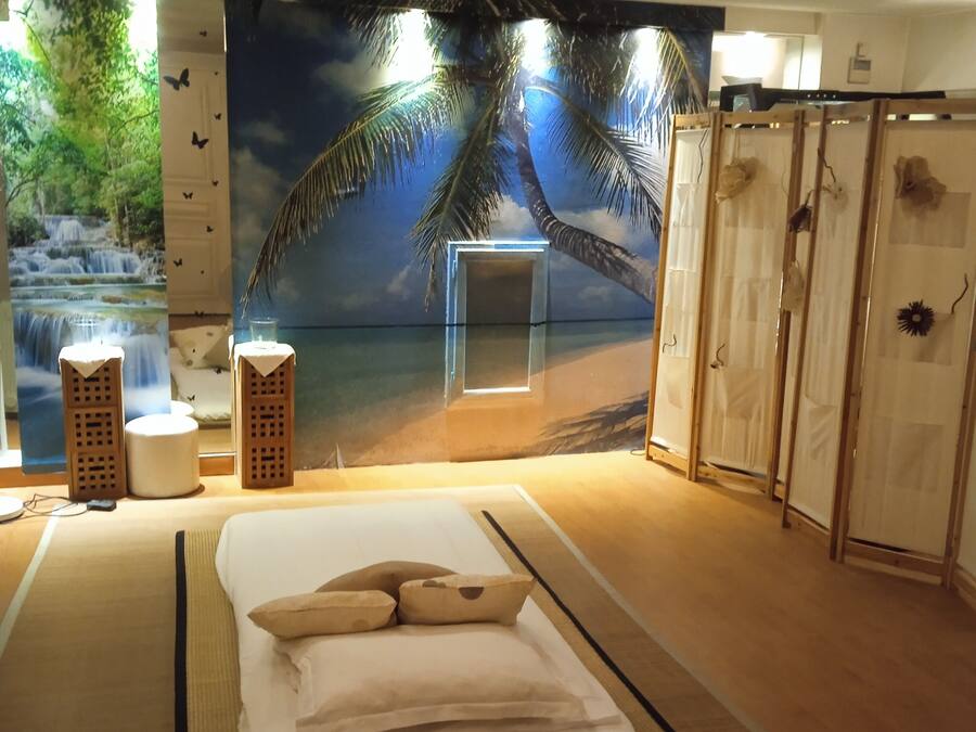 Quarto com cama, mesa de cabeceira, abajur e um mural na parede com uma cena de praia.