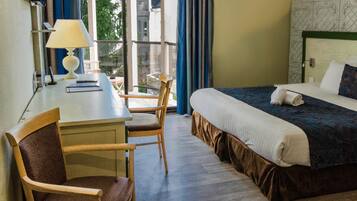Quarto de hotel com cama, escrivaninha com abajur, uma cadeira e vista através de uma grande janela.