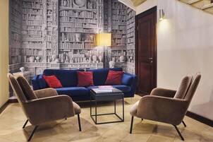 Quarto com um sofá azul, duas poltronas, uma mesinha e um mural de estante.