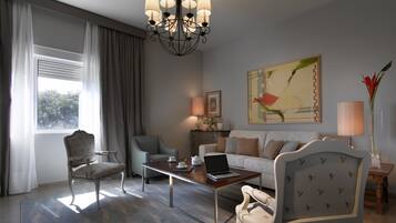 Sala de estar bem iluminada com um lustre moderno, um sofá, uma mesa de centro com um laptop e vista para o exterior por uma grande janela.