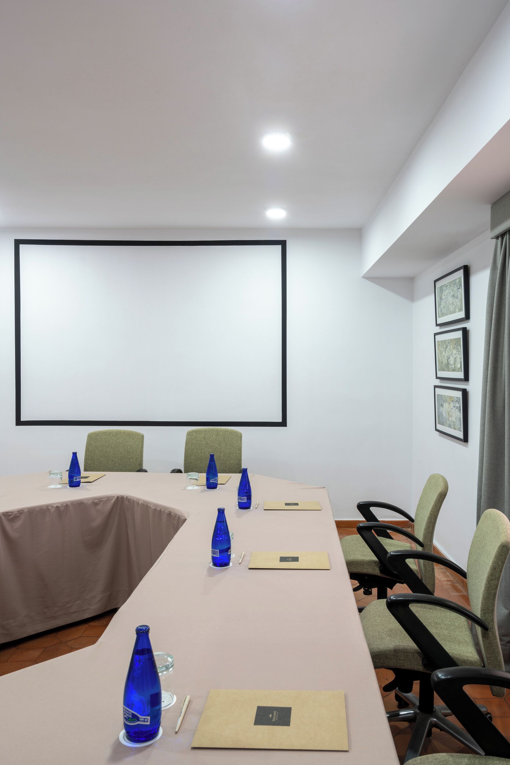 Uma sala de conferências com uma mesa comprida, cadeiras, uma tela de projetor e quadros nas paredes.