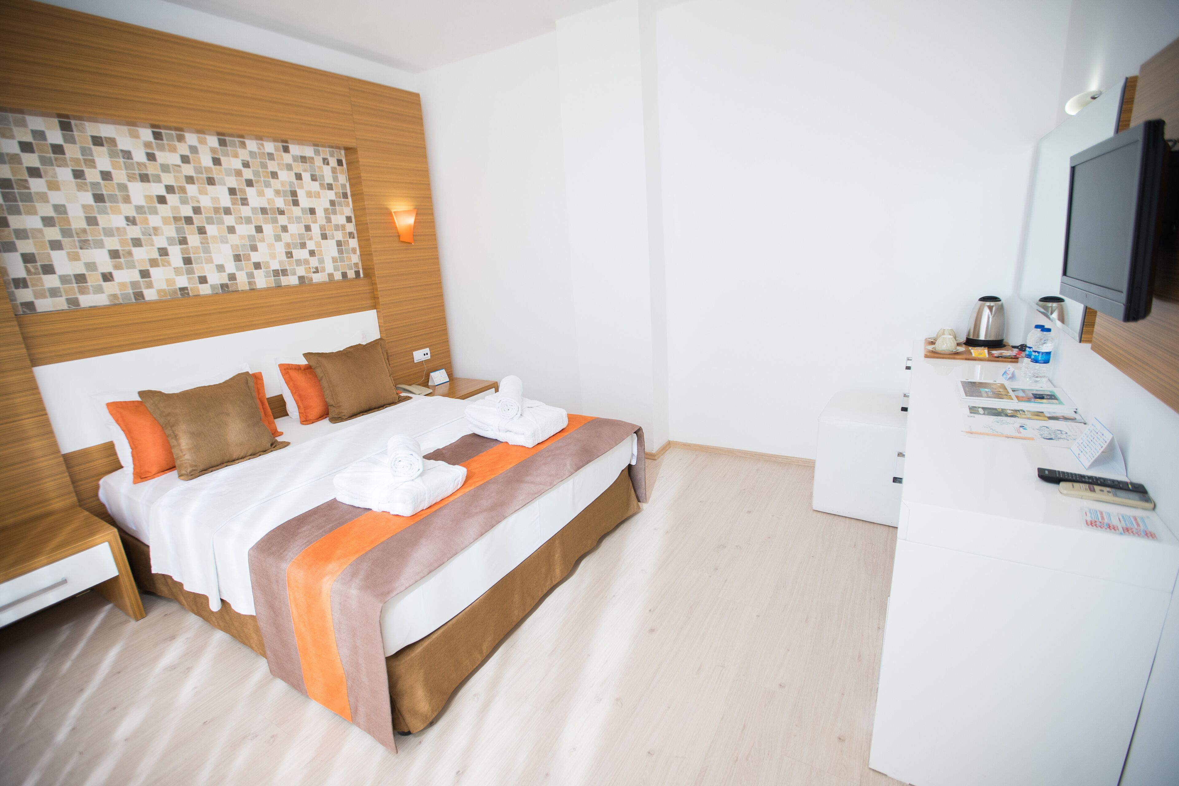Quarto de hotel com cama, mesa de cabeceira e escrivaninha com televisão de tela plana.