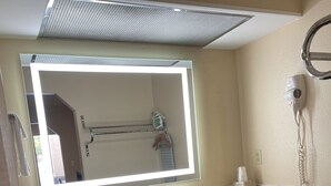 Casa de banho com um espelho grande, lavatório, um porta-toalhas, secador de cabelo e um cesto de lixo.