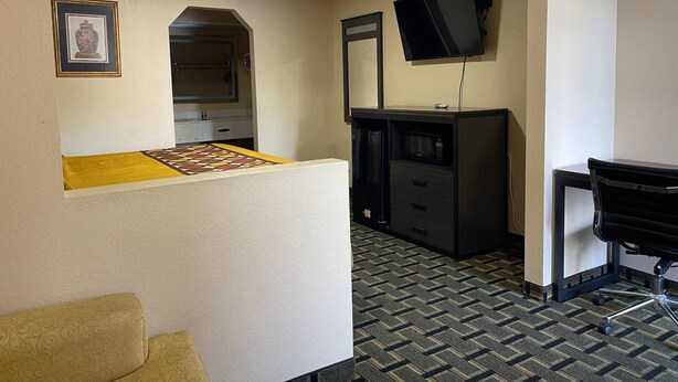 Quarto de hotel com sofá, escrivaninha com computador, TV fixada na parede e carpete estampado.