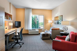 Quarto de hotel com escrivaninha, cadeira, sofá vermelho e janela com vista para árvores.