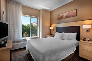 Quarto de hotel com uma cama grande, televisão de tela plana, aquecedor, mesa de cabeceira com abajur e janela com cortinas.