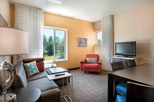 Quarto de hotel com sofá, poltrona, televisão e uma mesa pequena.