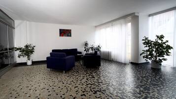 Um hall amplo com piso estampado, um conjunto de sofá azul e plantas em vasos.