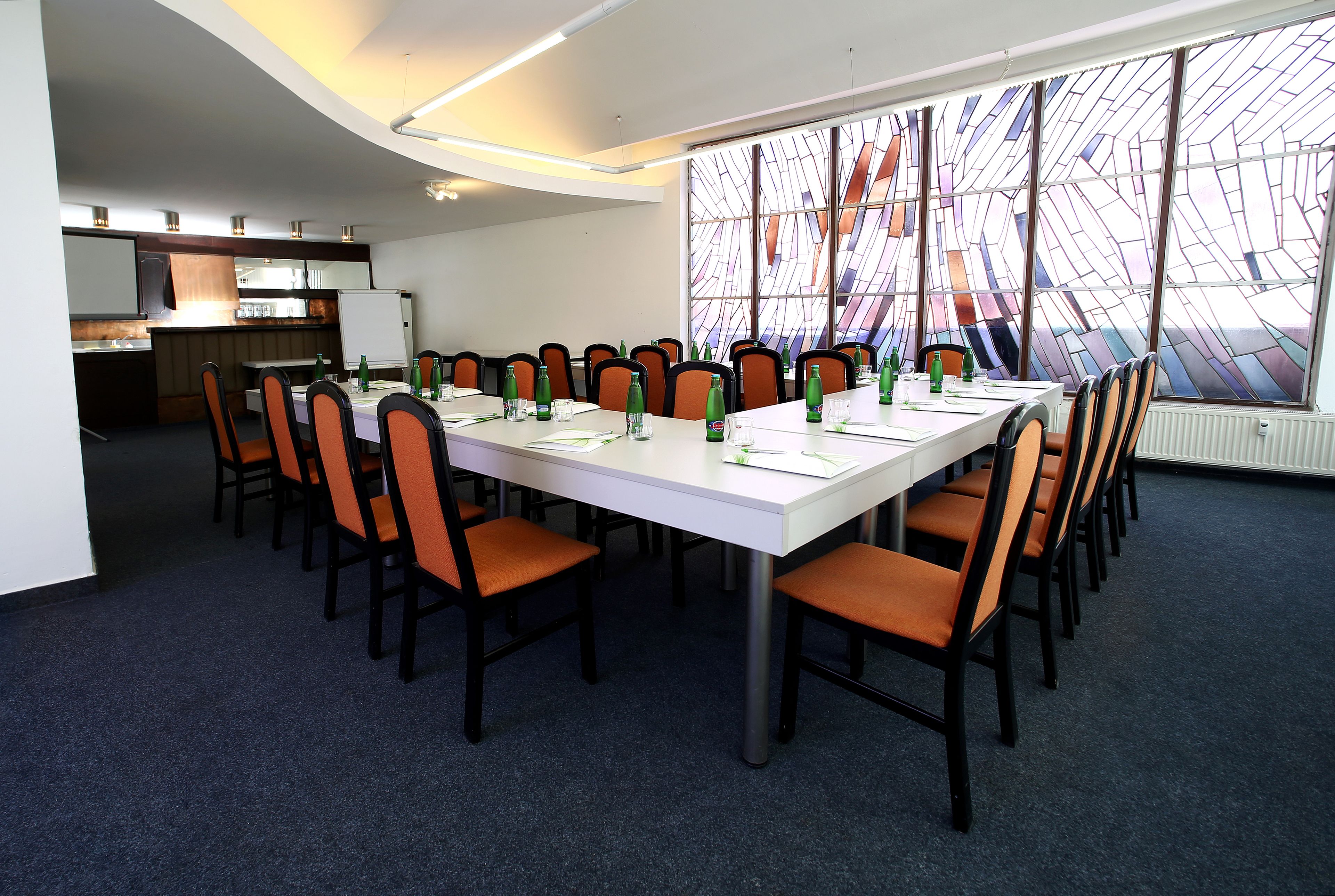 Sala de conferências com uma mesa comprida, cadeiras laranja e vista através de uma grande janela.